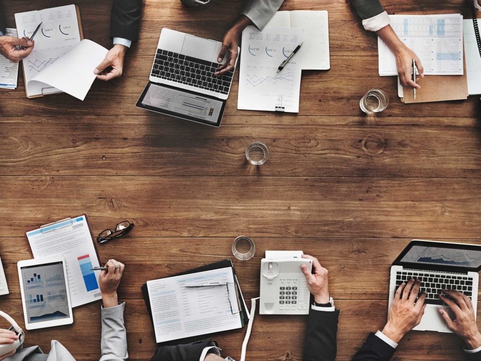 Team in der Geschäftsanalyse (Überkopfansicht). Auf dem Tisch liegen Finanzberichte, Grafiken und technische Geräte.